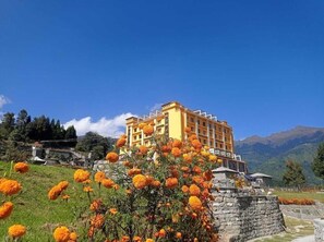 Um edifício amarelo com parede de pedra em frente, cercado por uma paisagem montanhosa.