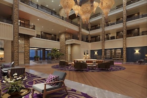 Um hall de hotel com vários níveis, uma área de estar central, pilares de pedra e um lustre.