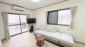 Uma sala de estar moderna com um sofá, uma mesa de centro redonda, uma TV de tela plana e janelas amplas com cortinas.