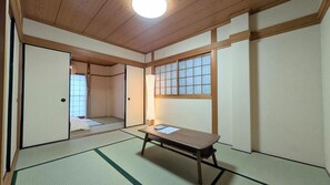 Um quarto japonês tradicional com tatames, portas deslizantes, uma mesa de madeira baixa e uma janela com vista.