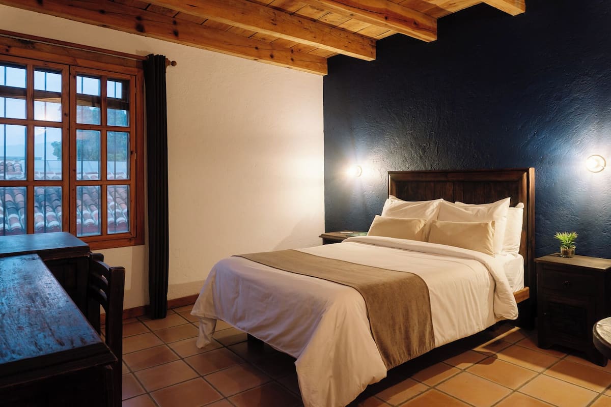 Quarto com cama, mesas de cabeceira, janela e vista para o exterior.