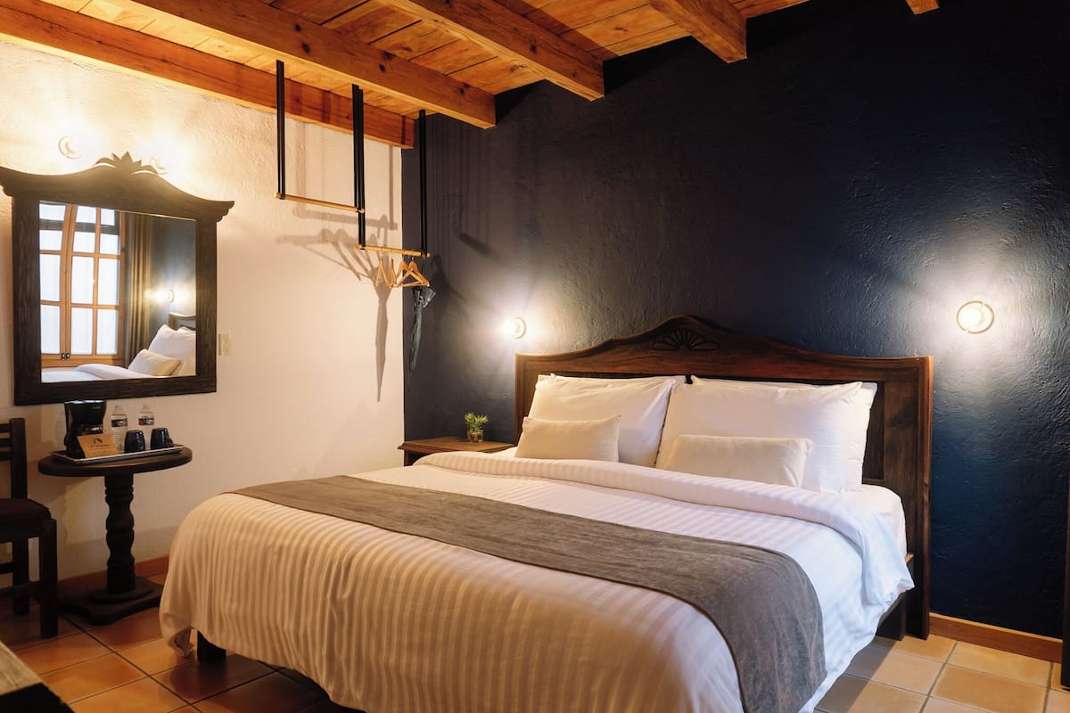 Uma cama bem arrumada com cabeceira de madeira, uma mesa de cabeceira com abajur e um espelho na parede.