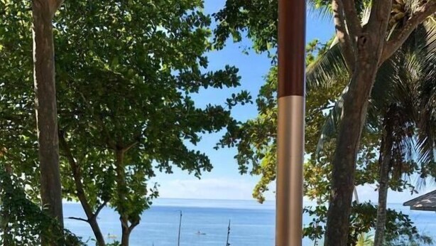 Uma mesa com itens de café da manhã, vista para o mar e vegetação tropical.