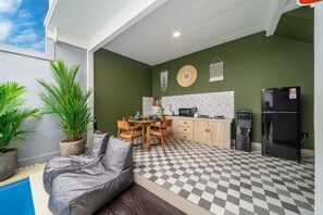 Uma cozinha compacta com piso xadrez, uma área de refeições com mesa e cadeiras, geladeira e bebedouro.