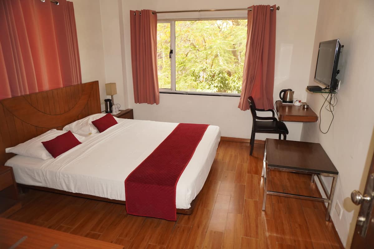 Quarto de hotel com cama, escrivaninha, cadeira, televisão e janela com cortinas.