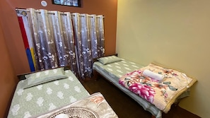 Quarto com duas camas de solteiro, cortina de chuveiro com estampas florais e televisão presa à parede.
