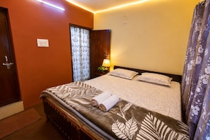 Quarto de hotel com cama, mesa de cabeceira, luminária, janela com cortinas e porta.