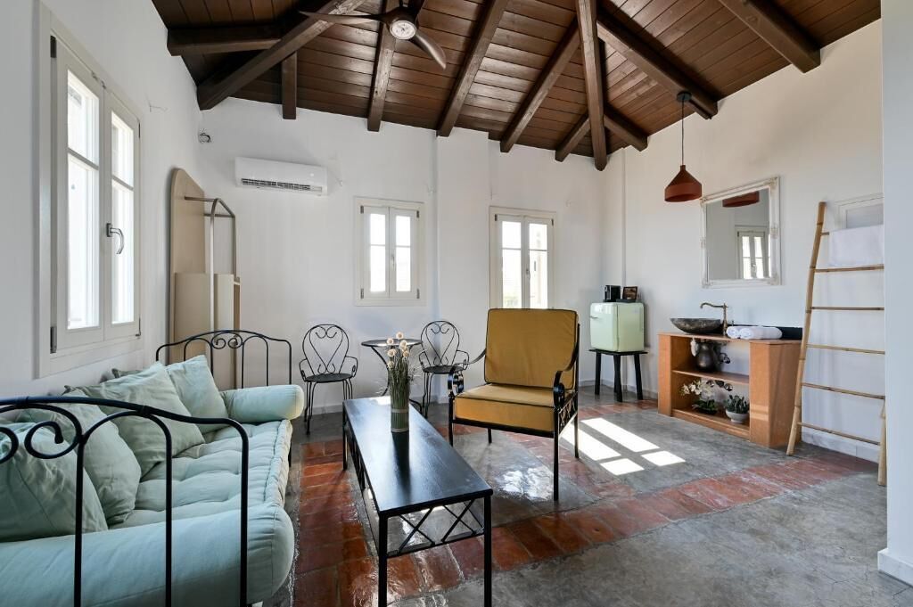 Quarto com teto de madeira, um sofá, uma mesa, uma cadeira, um armário pequeno e um espelho.