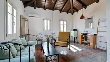 Quarto com teto de madeira, um sofá, uma mesa, uma cadeira, um armário pequeno e um espelho.