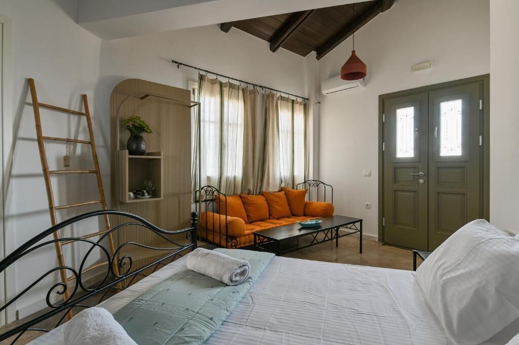 Quarto com cama, sofá, mesa pequena, guarda-roupa e janela com cortinas.