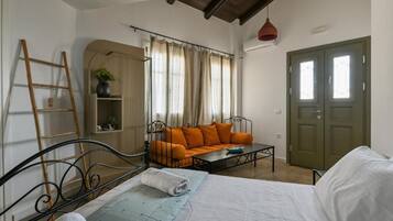 Quarto com cama, sofá, mesa pequena, guarda-roupa e janela com cortinas.