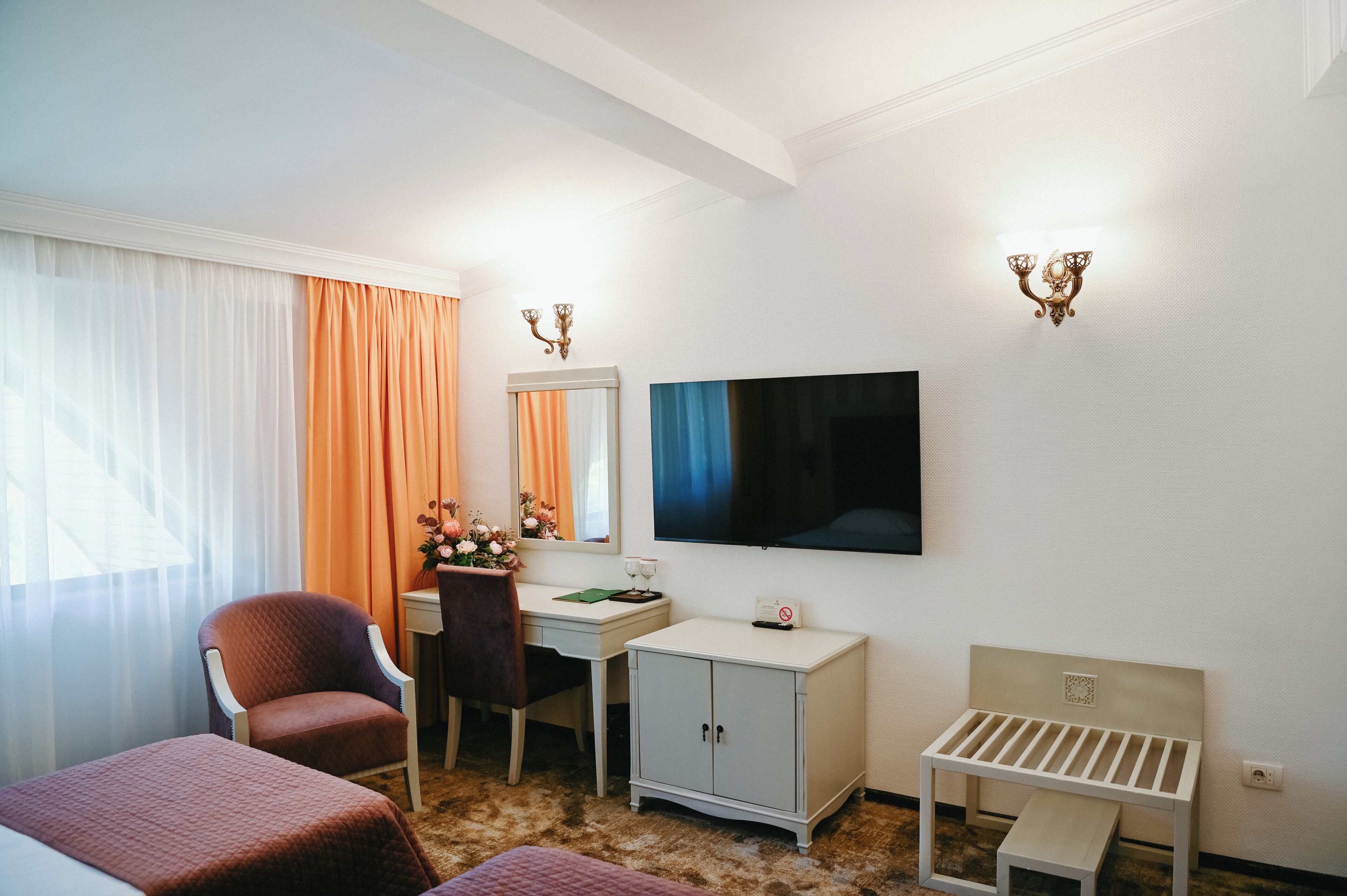 Quarto de hotel com cama, escrivaninha, cadeira, televisão e uma pequena mesa.