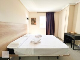 Quarto de hotel com cama, escrivaninha, cadeira, janela e cortina.