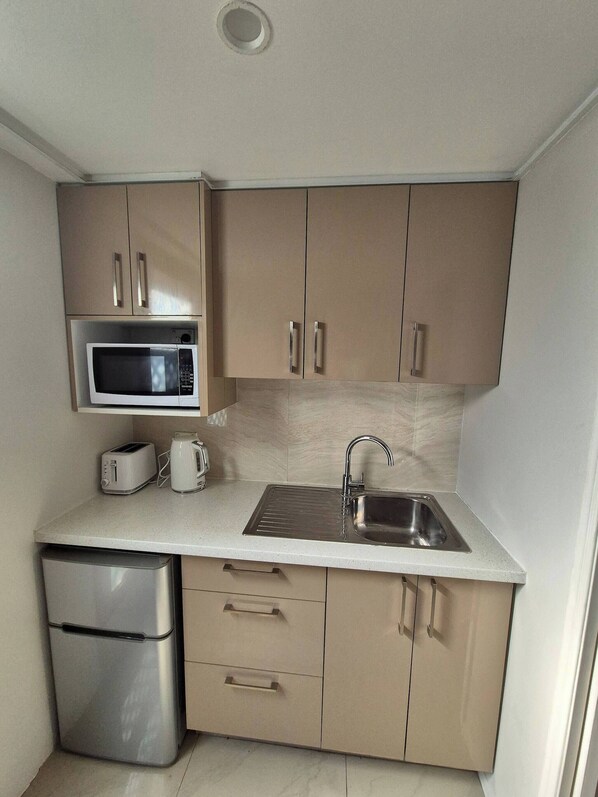 Uma cozinha compacta equipada com micro-ondas, torradeira, chaleira, pia e um frigorífico pequeno.