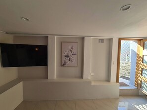 Interior moderno com televisão de tela plana, uma obra de arte floral emoldurada, iluminação embutida no teto e uma porta que dá para o exterior.