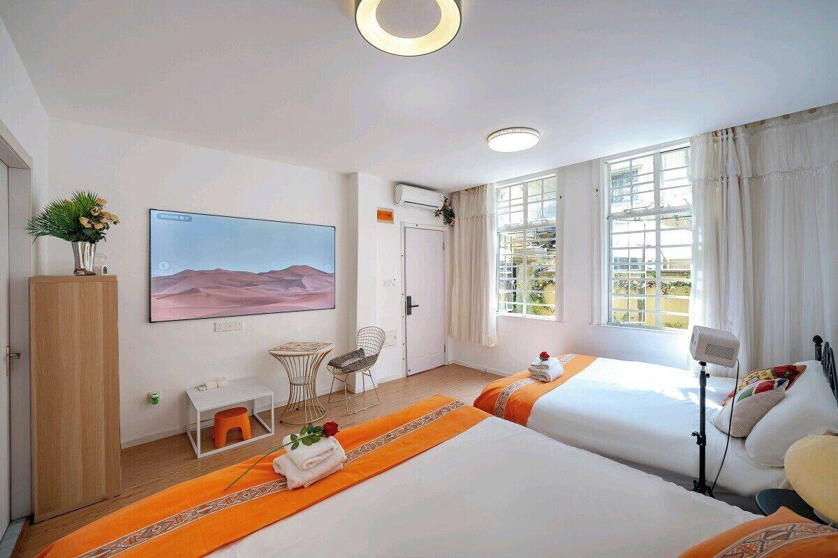 Quarto de hotel com duas camas, uma escrivaninha, uma cadeira, uma televisão e uma janela com cortinas.