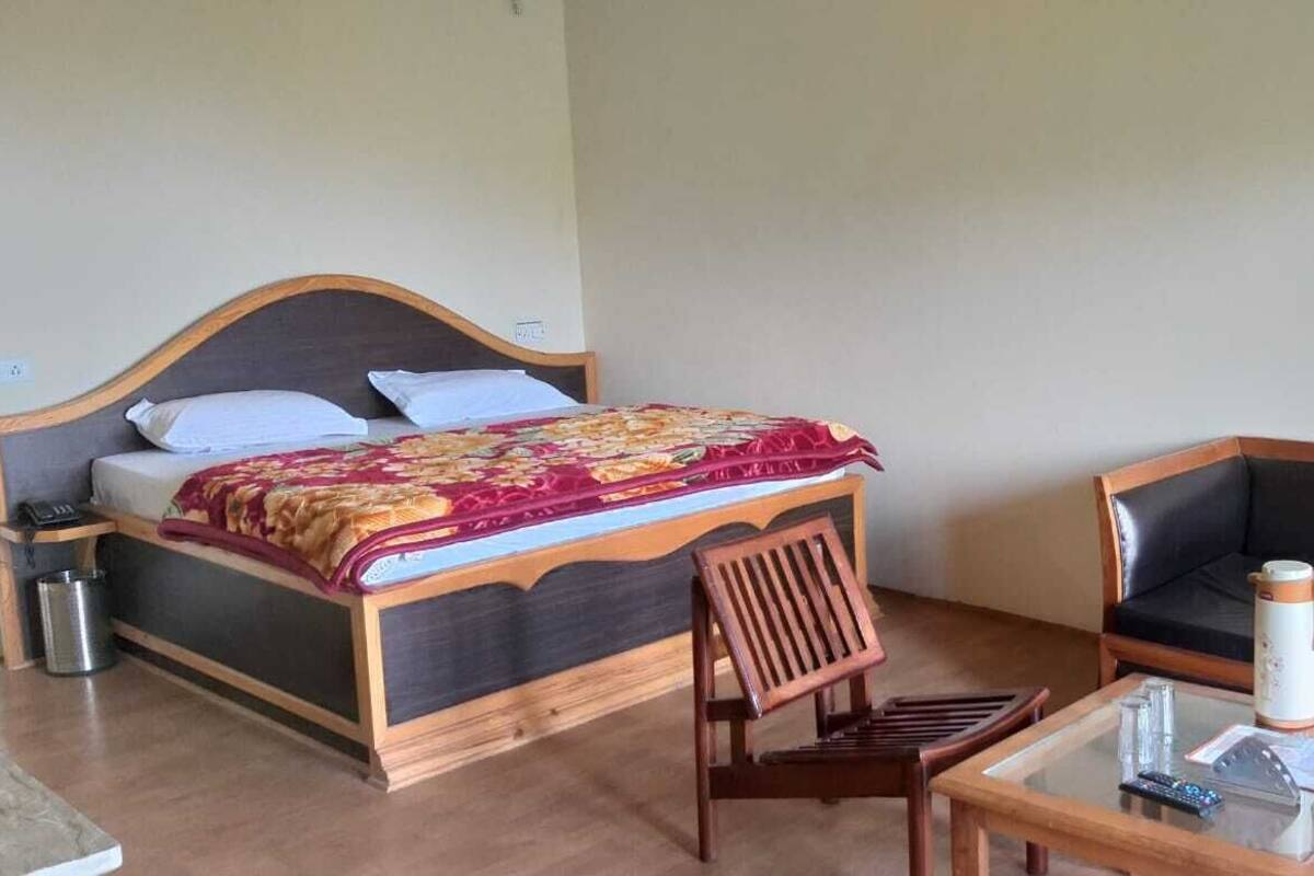 Um quarto com uma cama, uma cadeira de madeira, um sofá, uma mesinha de cabeceira e um abajur.