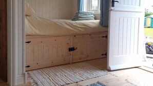 Quarto com cama, janela com cortinas, porta e uma pequena janela acima da porta.