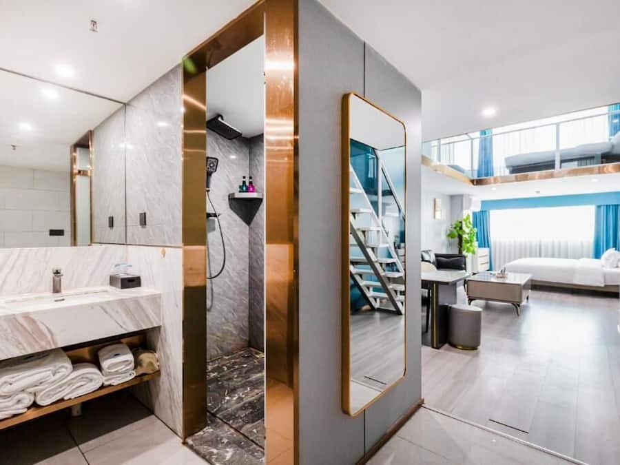 Quarto de hotel moderno com casa de banho em mármore, um espelho grande, uma escadaria e uma varanda.