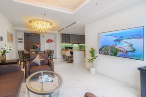 Uma sala de estar moderna com área de jantar, cozinha e uma grande pintura de paisagem costeira.