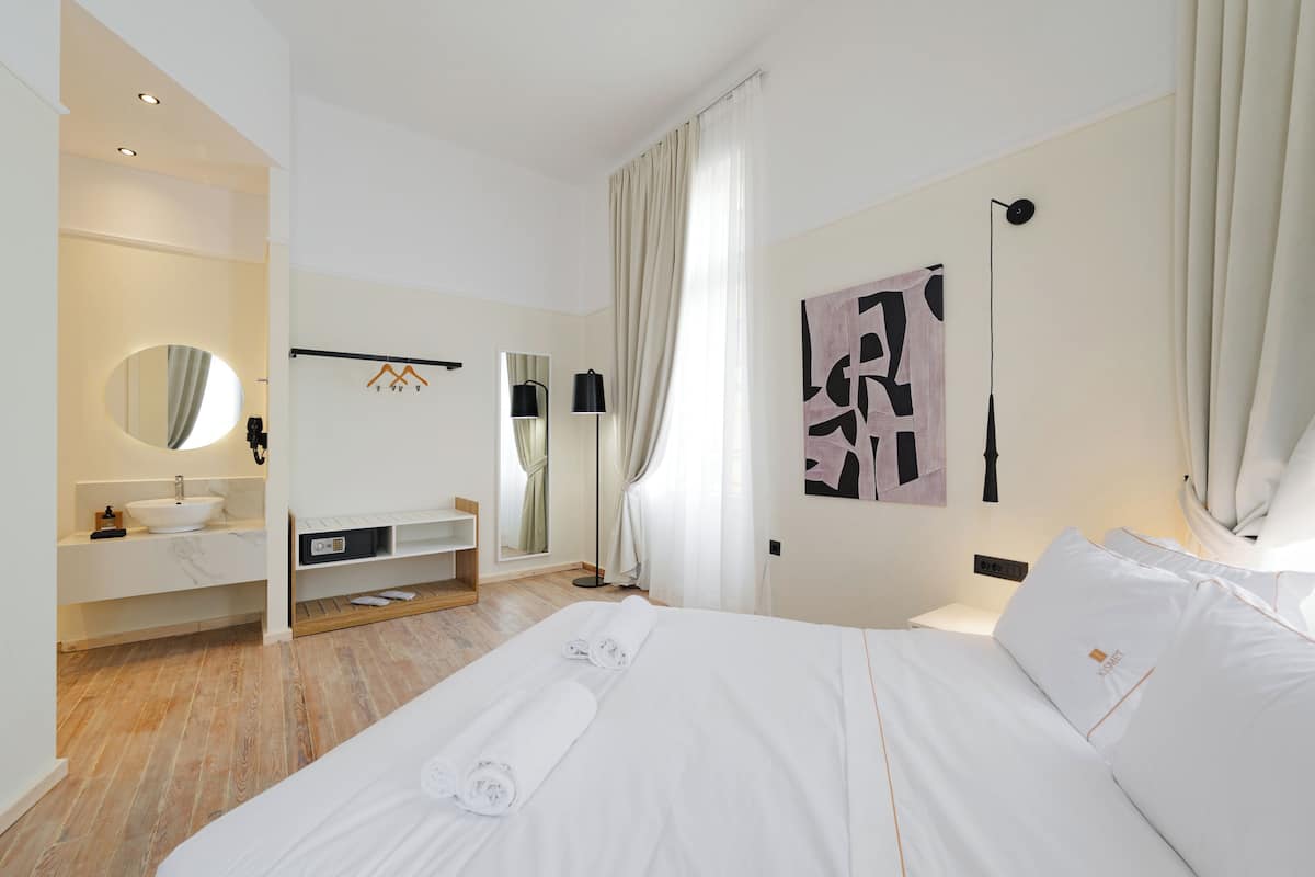 Quarto de hotel com cama, banheiro com pia, espelho e uma grande pintura abstrata na parede.