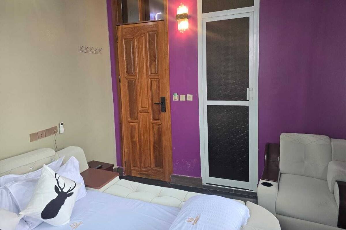 Um quarto com cama, uma cadeira, porta de madeira e janela com vista.