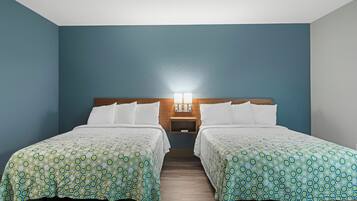 Quarto de hotel com duas camas, cabeceira de madeira, mesa de cabeceira com abajur e parede azul.