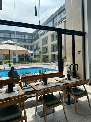 Um restaurante com área externa, vista para a piscina e um edifício moderno ao fundo.