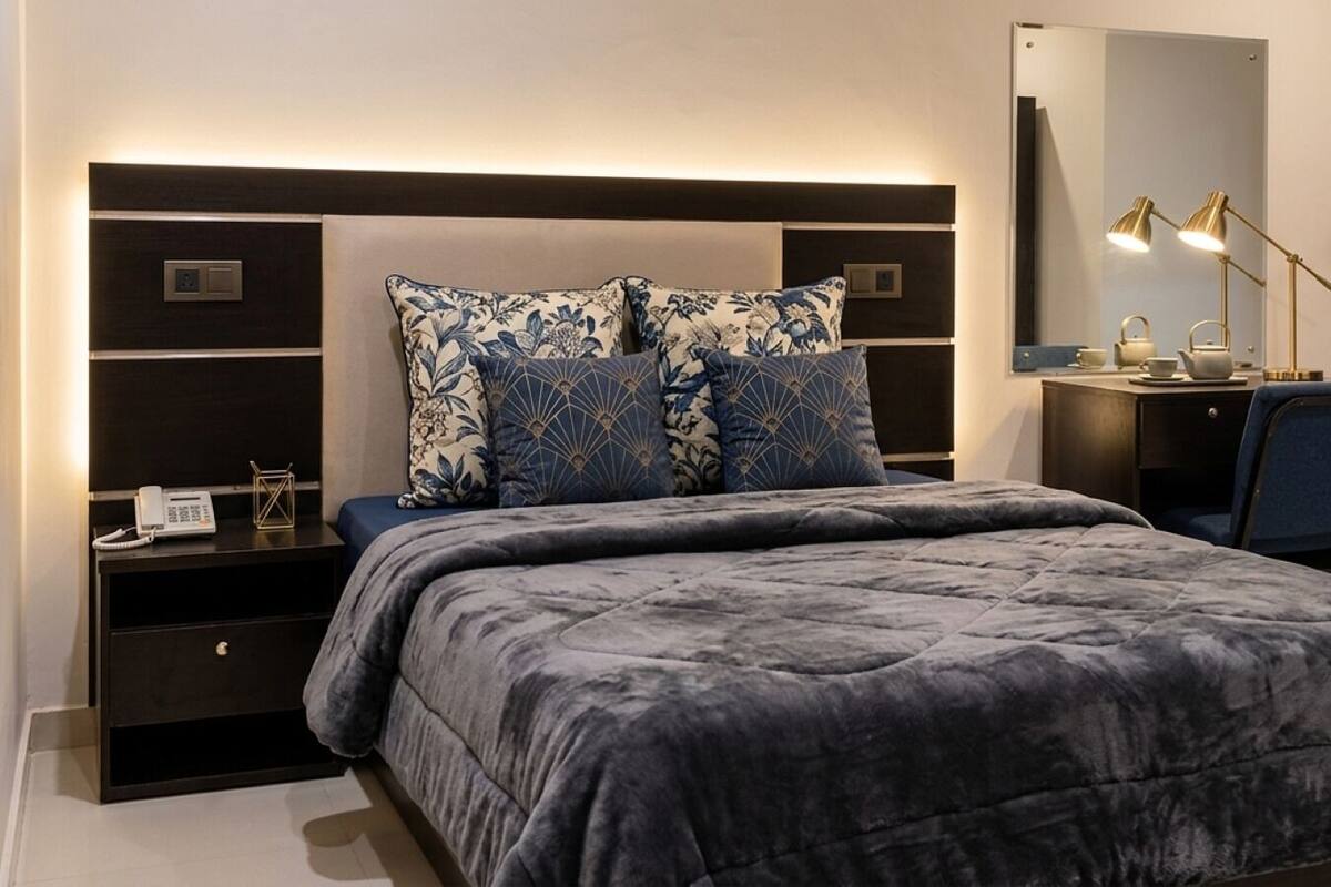 Quarto com cama, mesas de cabeceira, escrivaninha e espelho.