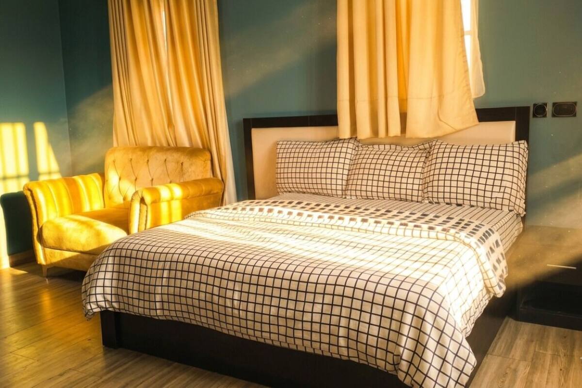 Um quarto com cama, cortinas, uma cadeira e mesa de cabeceira.
