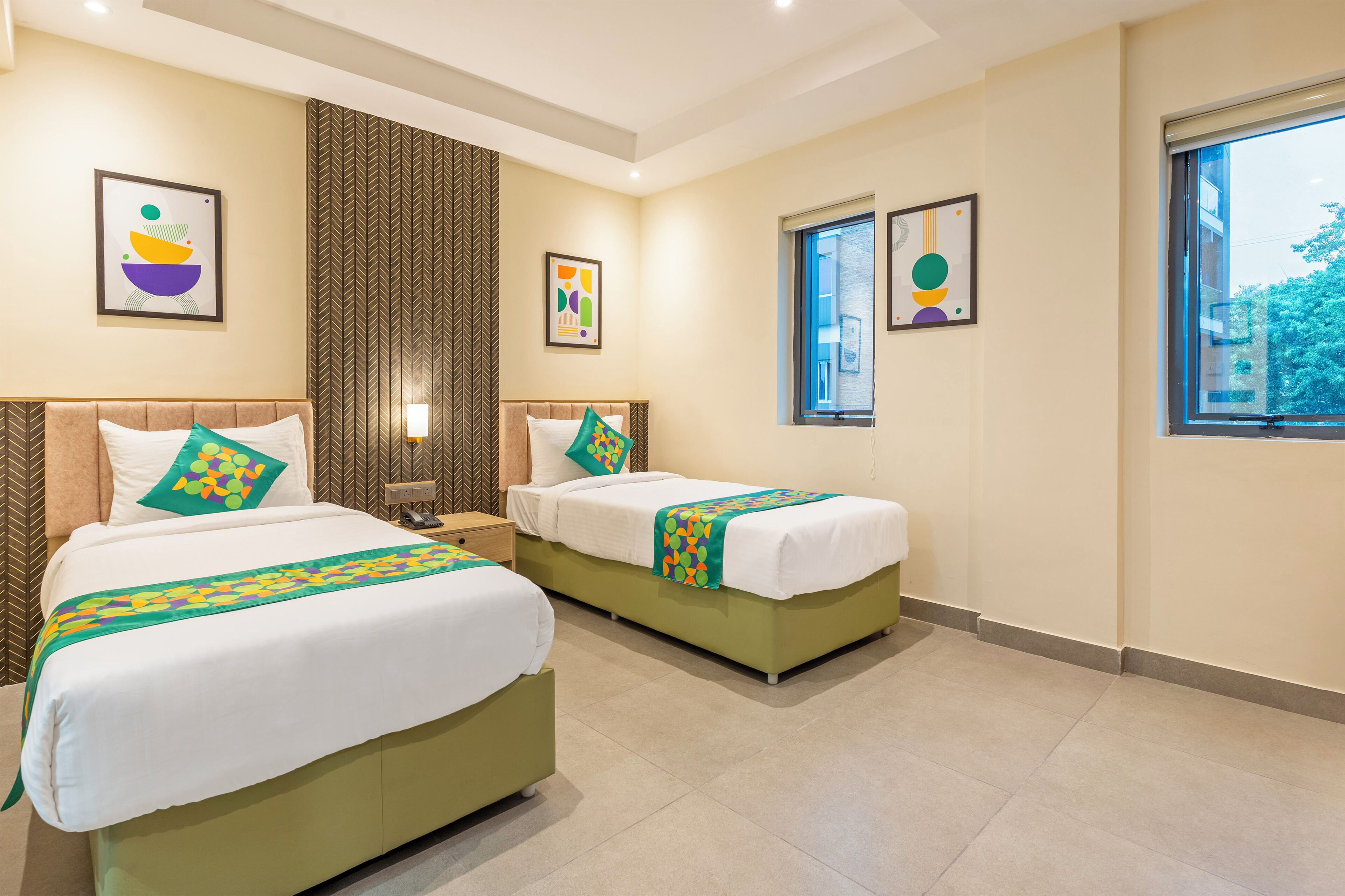 Quarto de hotel com duas camas, uma mesa de cabeceira, uma janela e obras de arte nas paredes.