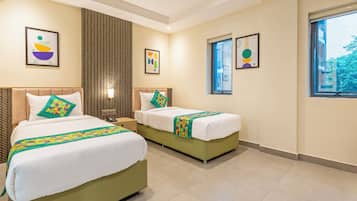Quarto de hotel com duas camas, uma mesa de cabeceira, uma janela e obras de arte nas paredes.