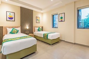 Quarto de hotel com duas camas, uma mesa de cabeceira, uma janela e obras de arte nas paredes.