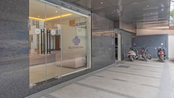 Entrada de um edifício moderno com portas de vidro, uma placa com a inscrição 'EMPURRAR' e três scooters estacionadas na frente.