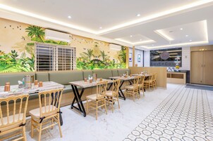 Um restaurante com um mural tropical, cadeiras de madeira e chão de mármore.