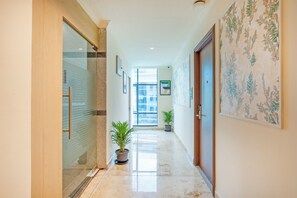 Um corredor com porta de vidro, plantas em vasos, obras de arte emolduradas e vista para o exterior.