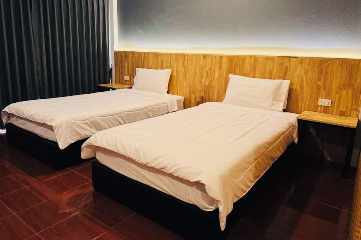 Duas camas com cabeceiras de madeira, cortinas escuras e chão de azulejos.