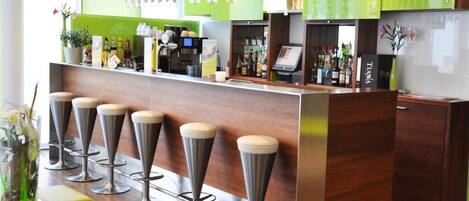 Uma área de bar com banquetas, balcão e prateleiras com garrafas e copos.