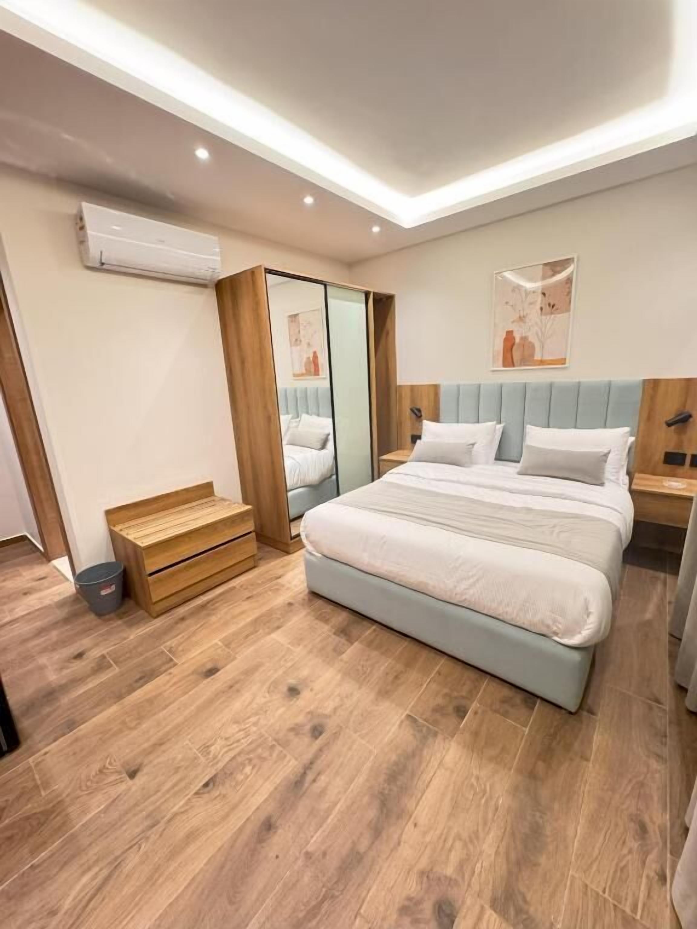 Quarto moderno com cama grande, soalho de madeira, guarda-roupa e luminária no teto.