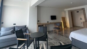 Quarto de hotel moderno com sofá, mesa de jantar, cadeiras, televisão e cama.
