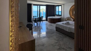 Quarto de hotel moderno com uma cama grande, área de estar com vista e sala de jantar.