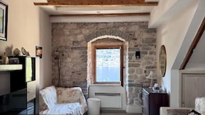 Uma sala de estar acolhedora com parede de pedra, vigas de madeira, lareira e vista para o exterior.