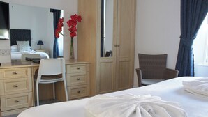 Quarto de hotel com cama, escrivaninha, cadeira, guarda-roupa e espelho.