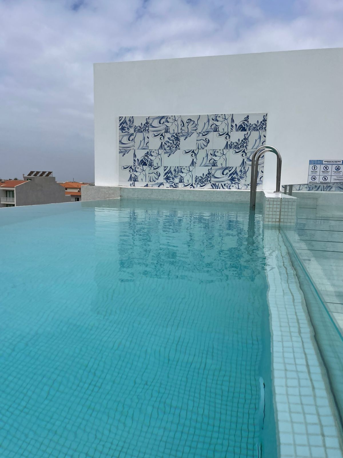Piscina com parede revestida em azulejo com padrões florais, escada de metal e borda em azulejo.