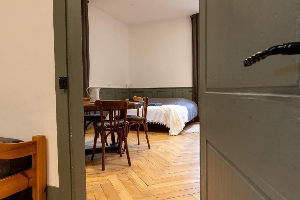 Um quarto com uma cama, uma cadeira de madeira, uma mesa e uma porta.
