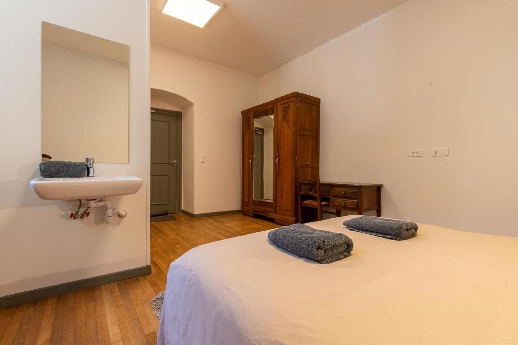 Quarto com cama, guarda-roupa de madeira, espelho e pia.