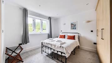 Quarto com cama, janela com cortinas, mesa de cabeceira, cadeira e guarda-roupa.