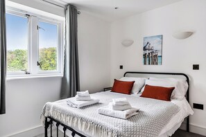 Quarto com cama, janela com cortinas, pintura na parede e vista para o verde lá fora.