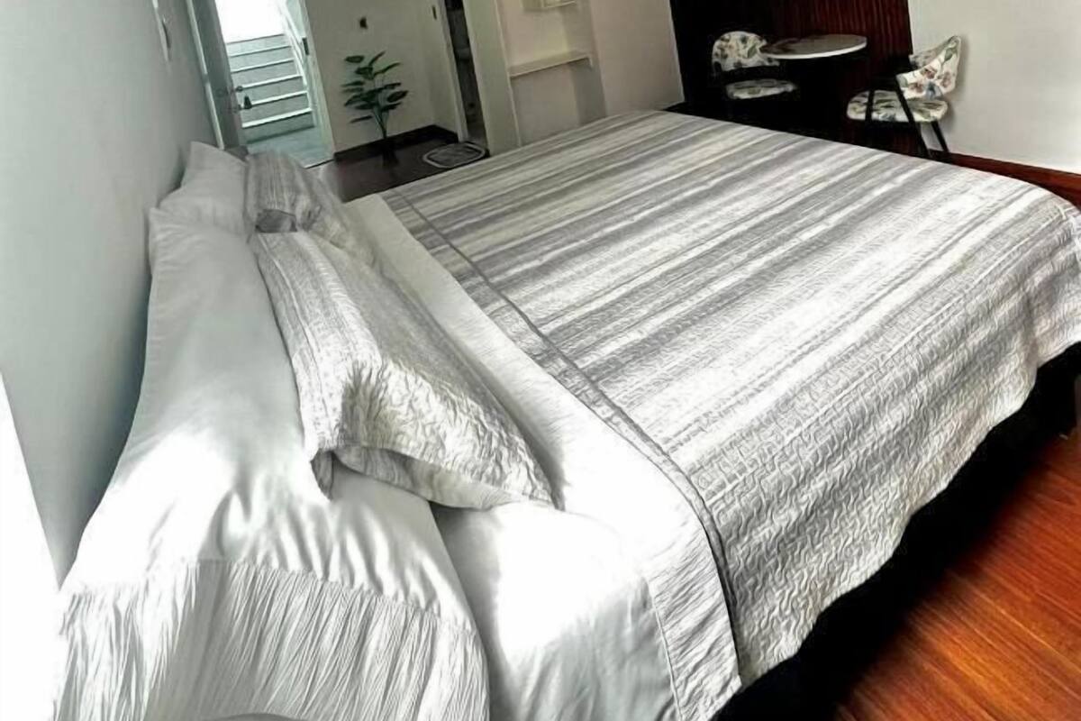 Quarto com uma cama grande, uma mesa pequena e uma cadeira.