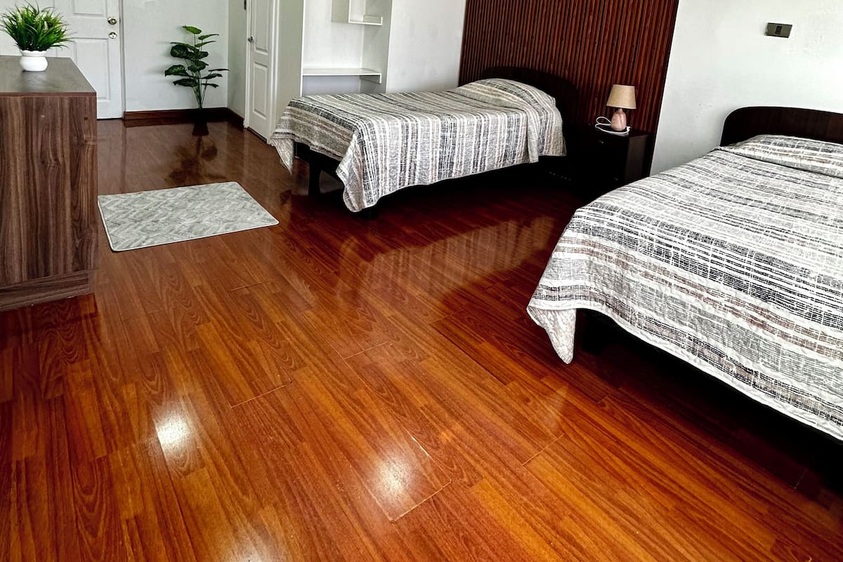 Quarto com duas camas, piso de madeira, guarda-roupa e planta pendente.